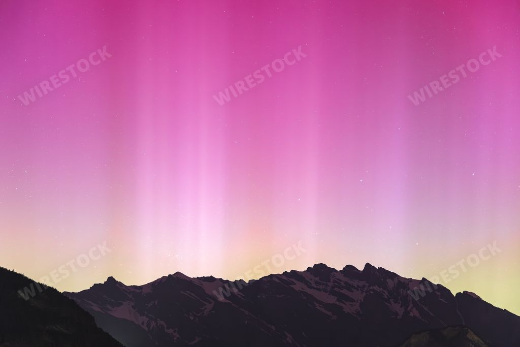 Pink northern lights landscape over a mountain range in the Swiss Alps ...